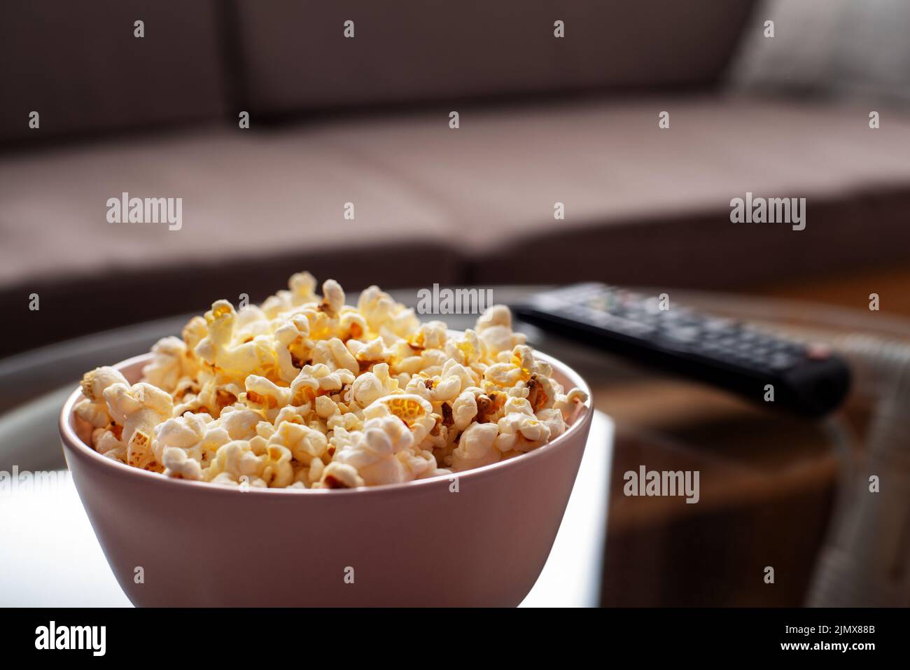 Bowl with popcorn and tv remote control on glass table near sofa Stock ...