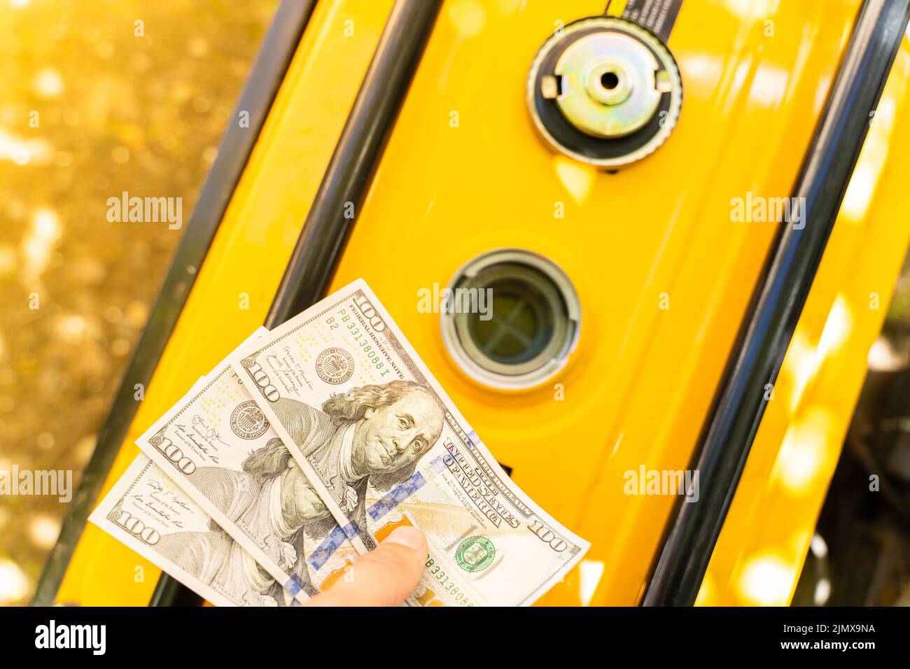 A hand stretches a stack of hundred dollar bills into the filler neck ...