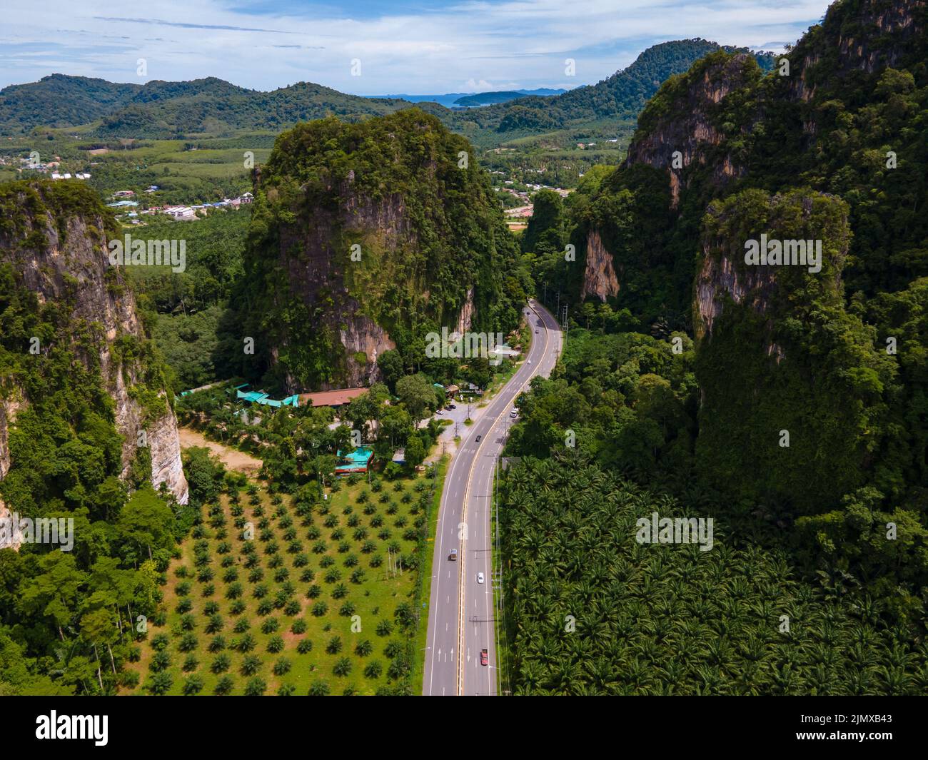Beautiful road with traffic between palm trees and limestone mountains ...