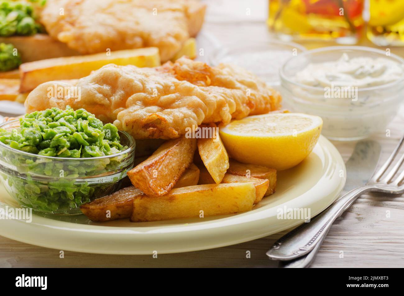 Traditional British street food fish and chips with tartar sauce and mushy peas on paper plate ...