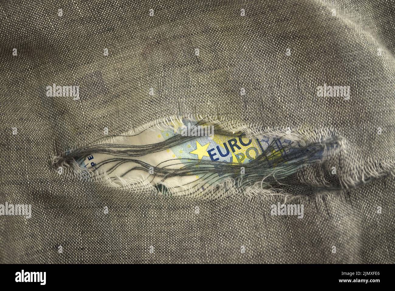 Euro banknote viewed through a hole in torn grey fabric in a financial ...