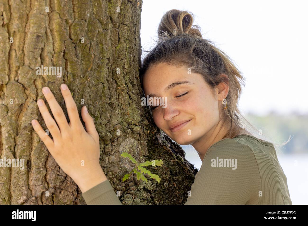 Contented young woman hugging a large tree with a blissful expression ...