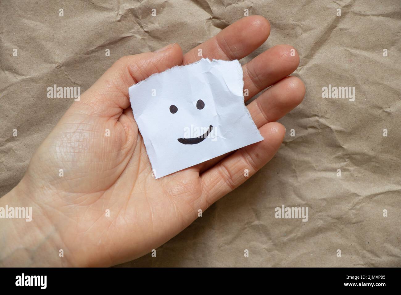 a cheerful emoticon is drawn on a piece of paper in the hands of a ...