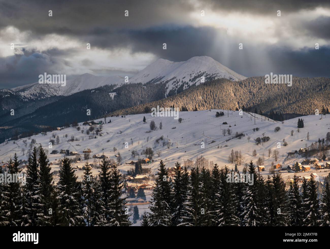 Small alpine village and winter snowy mountains in sunrise sun rays ...