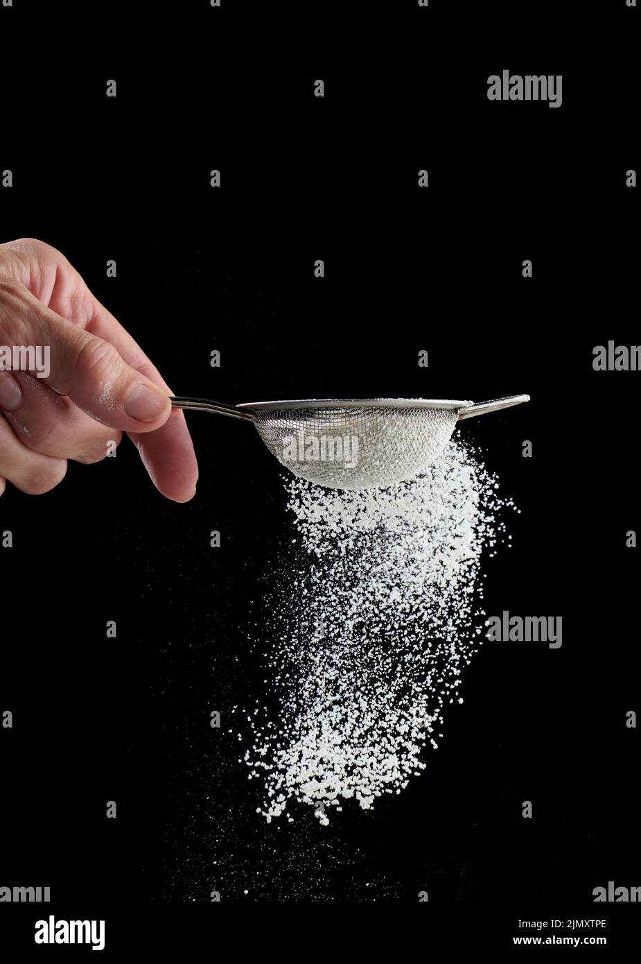 Female hand holds a metal strainer with powdered sugar. Particles fly ...