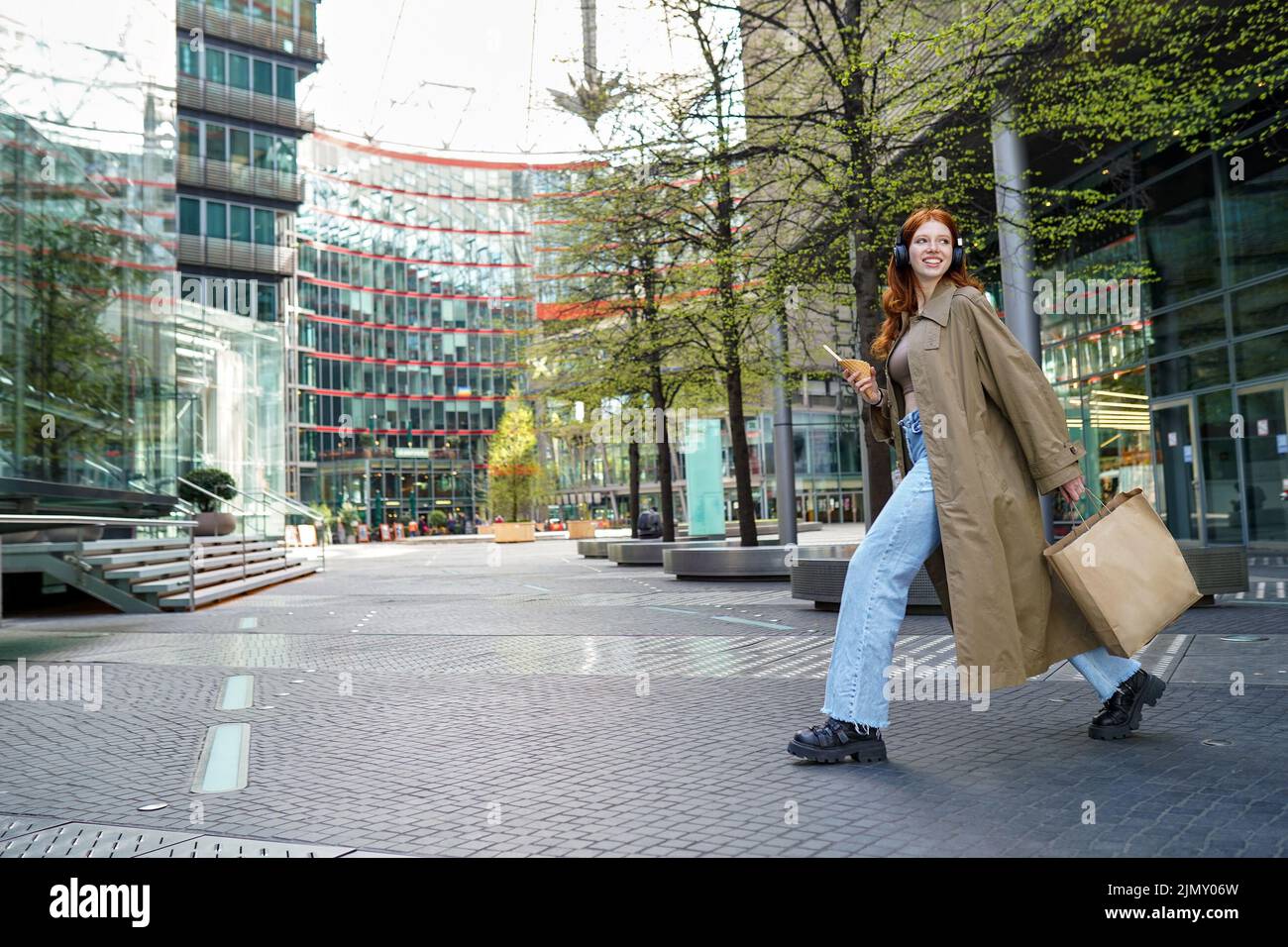 Happy fashion girl model holding shopping bags walking on busy big city ...