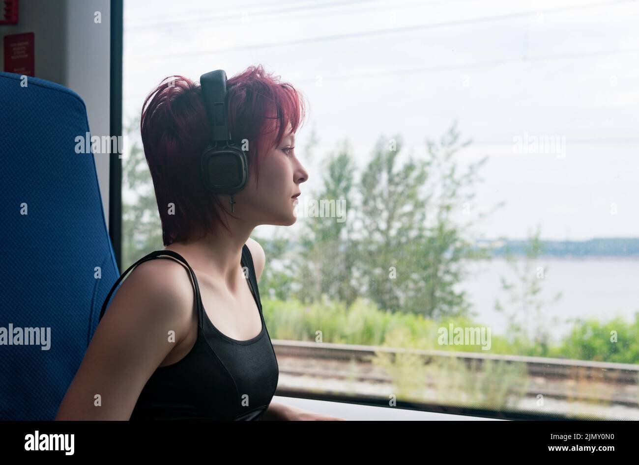 girl with headphones rides in a moving suburban train and looks out the ...