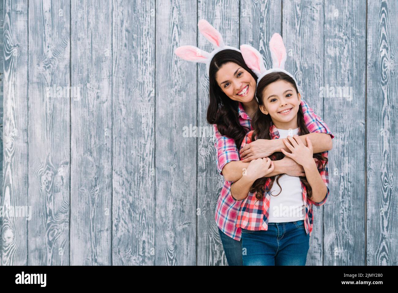 Smiling portrait mother embracing her daughter from front wooden ... Smiling portrait mother embracing her daughter from front wooden ...