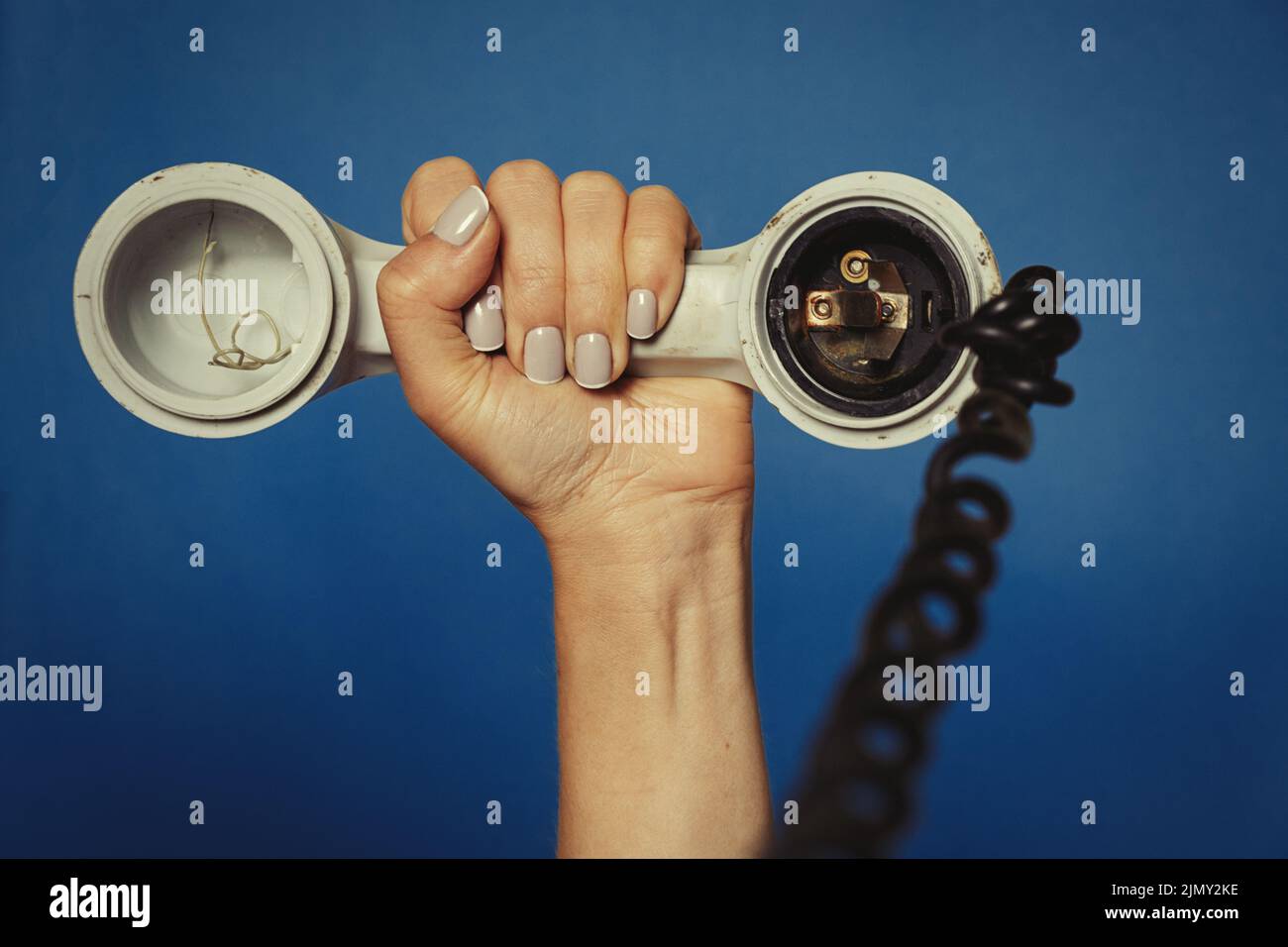 female hand holding an old broken telephone receiver on a wire on an ...