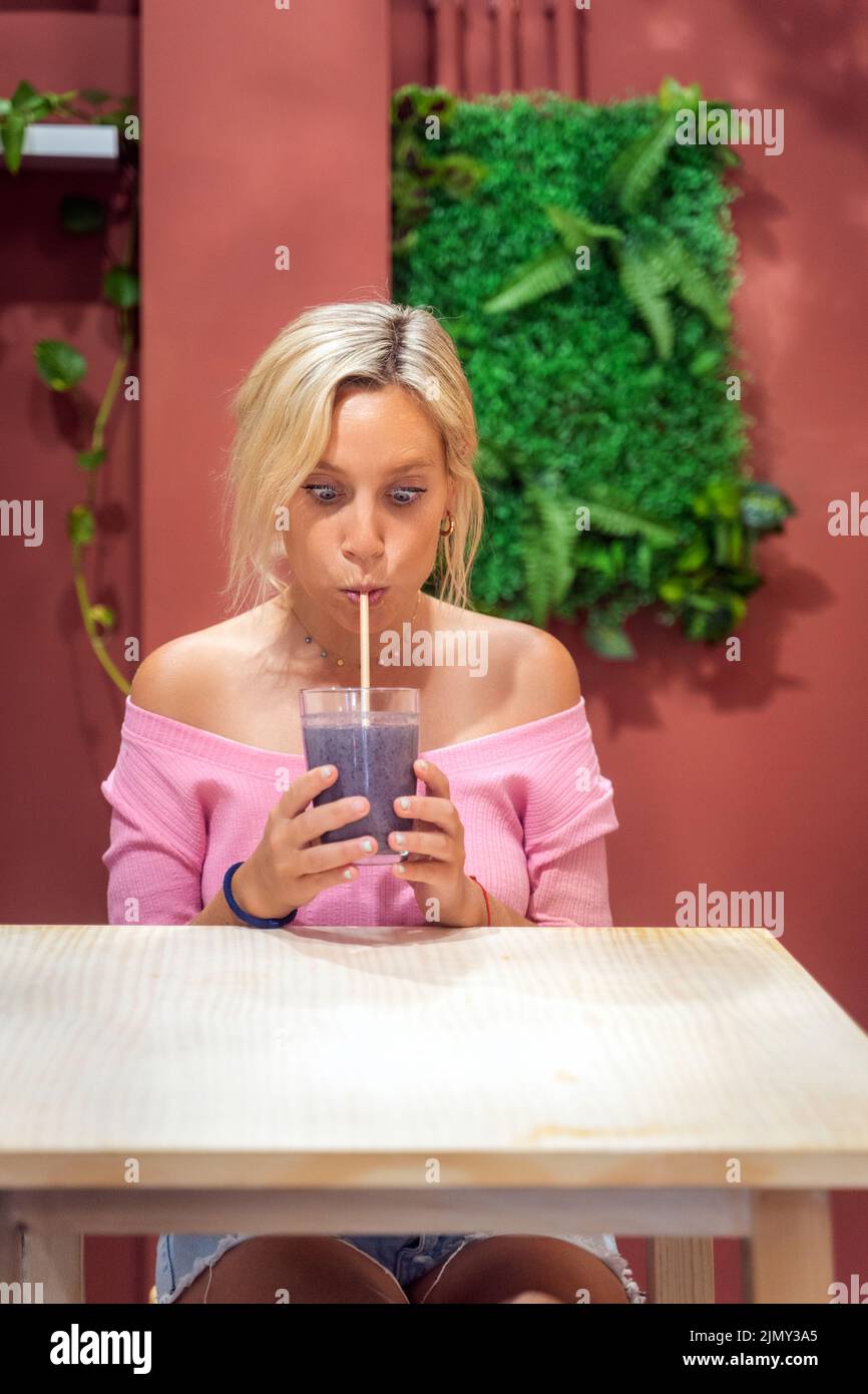 Young woman enjoying drinking a delicious smoothie sitting indoors in a ...