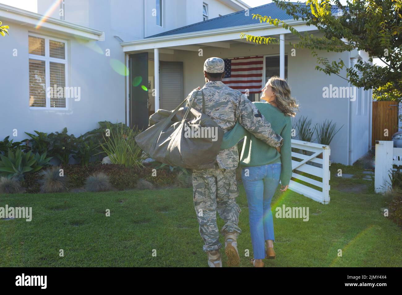 Rear view of solider with arm around multiracial woman carrying ...