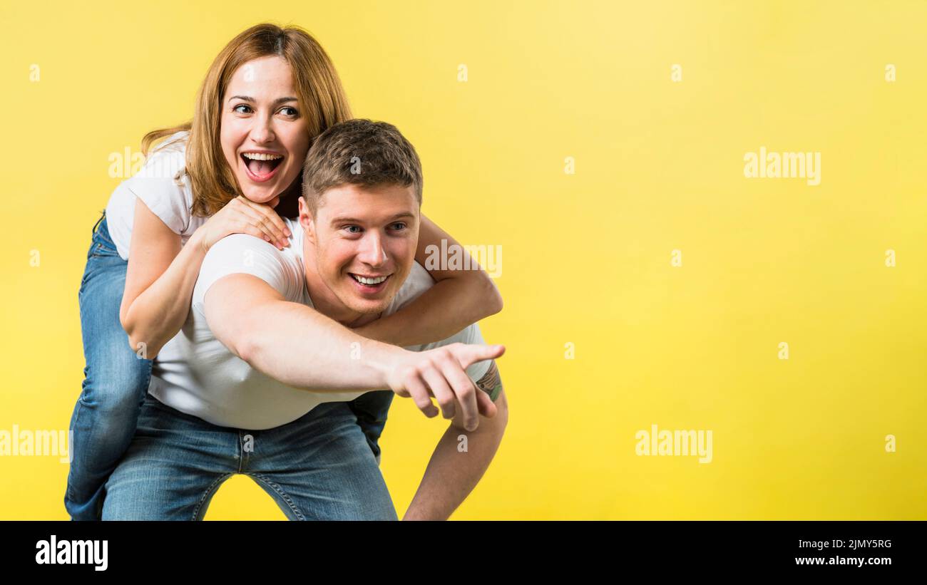Man giving her laughing girlfriend piggyback ride pointing camera ...