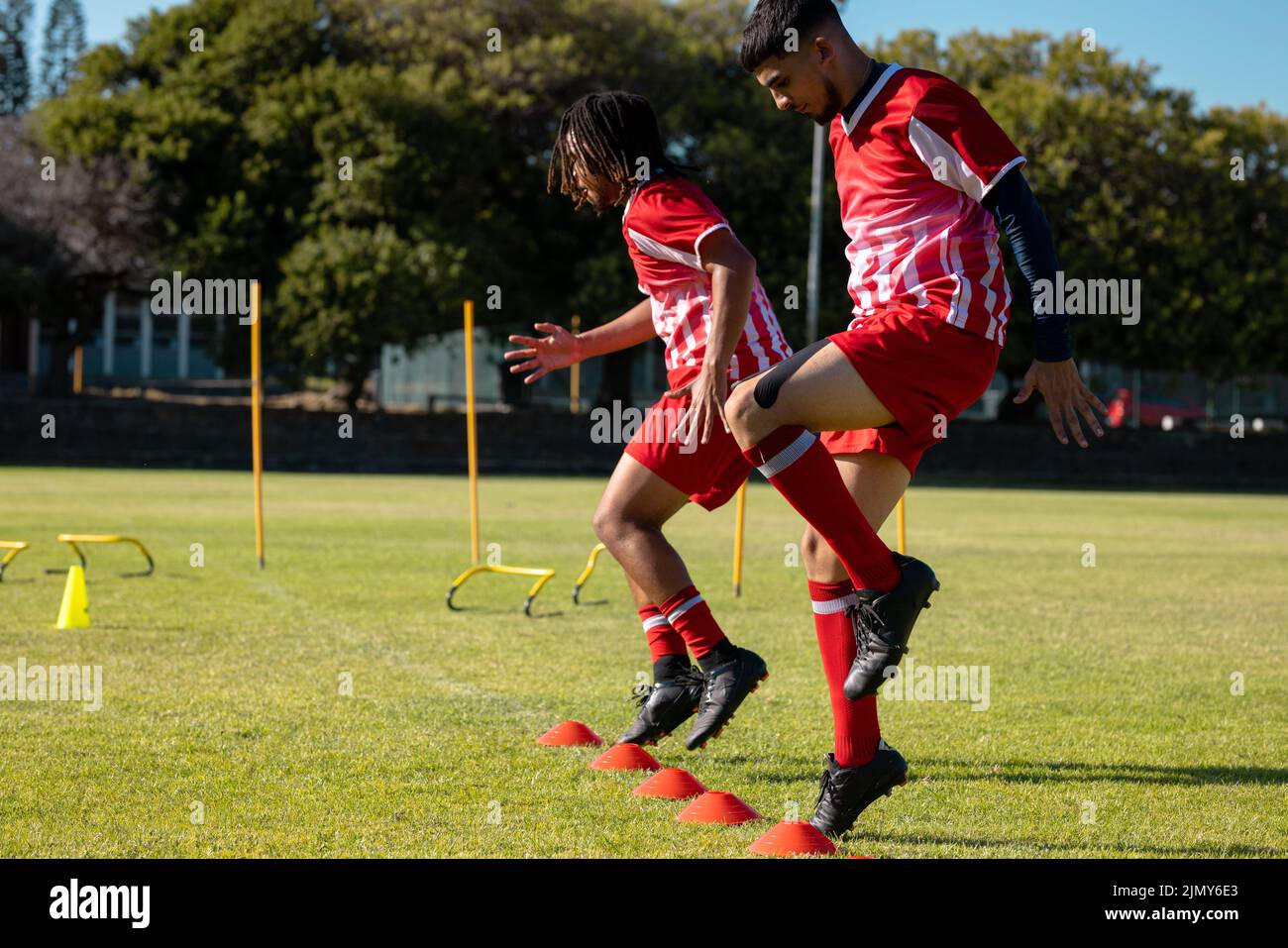 Side view of multiracial male players jumping on disc cones over grassy ...
