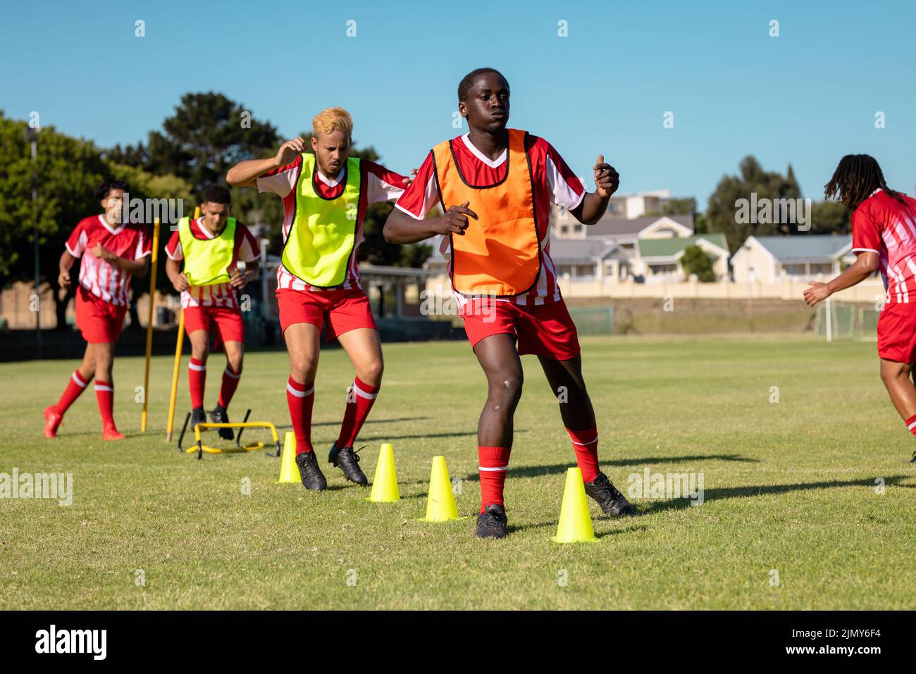 Multiracial male players in red jerseys running around yellow cones at ...