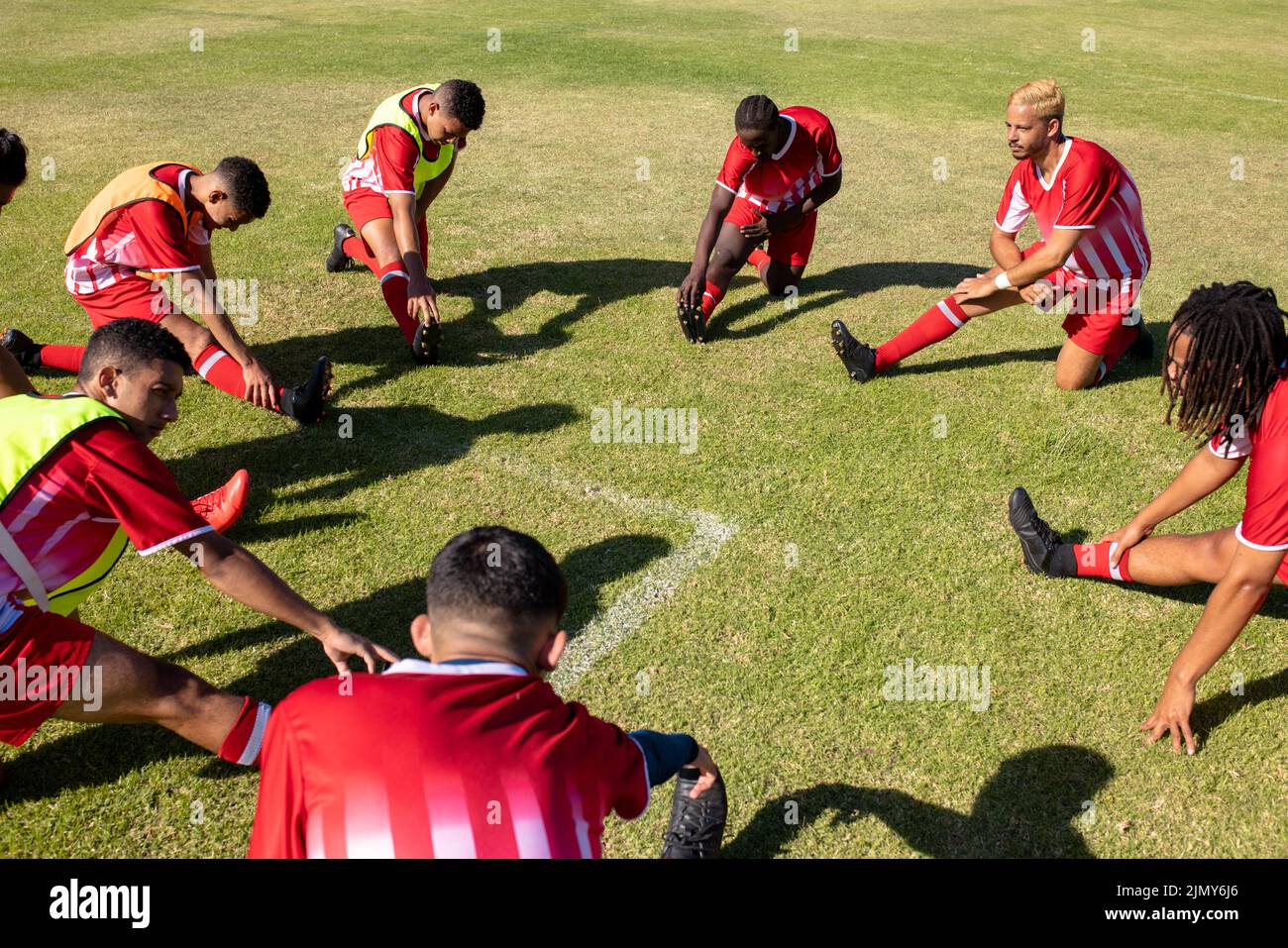 High angle view of multiracial male athletes stretching legs on grassy ...