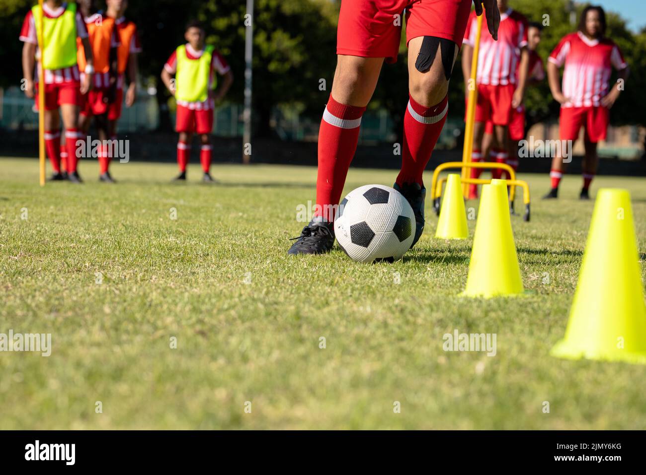 Low section of multiracial male player kicking ball between cones while ...
