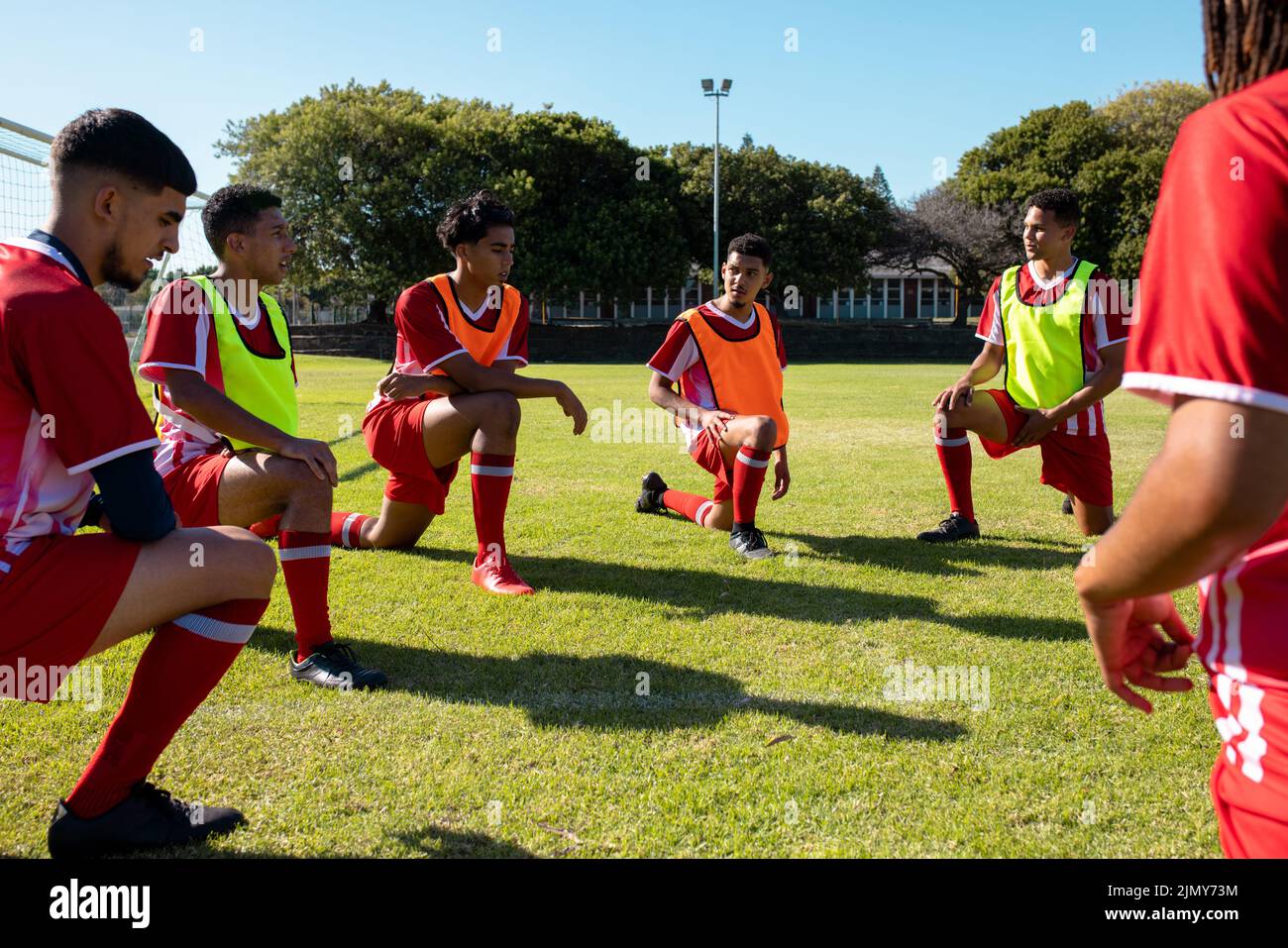 Multiracial male soccer team players stretching legs on grassy field in ...