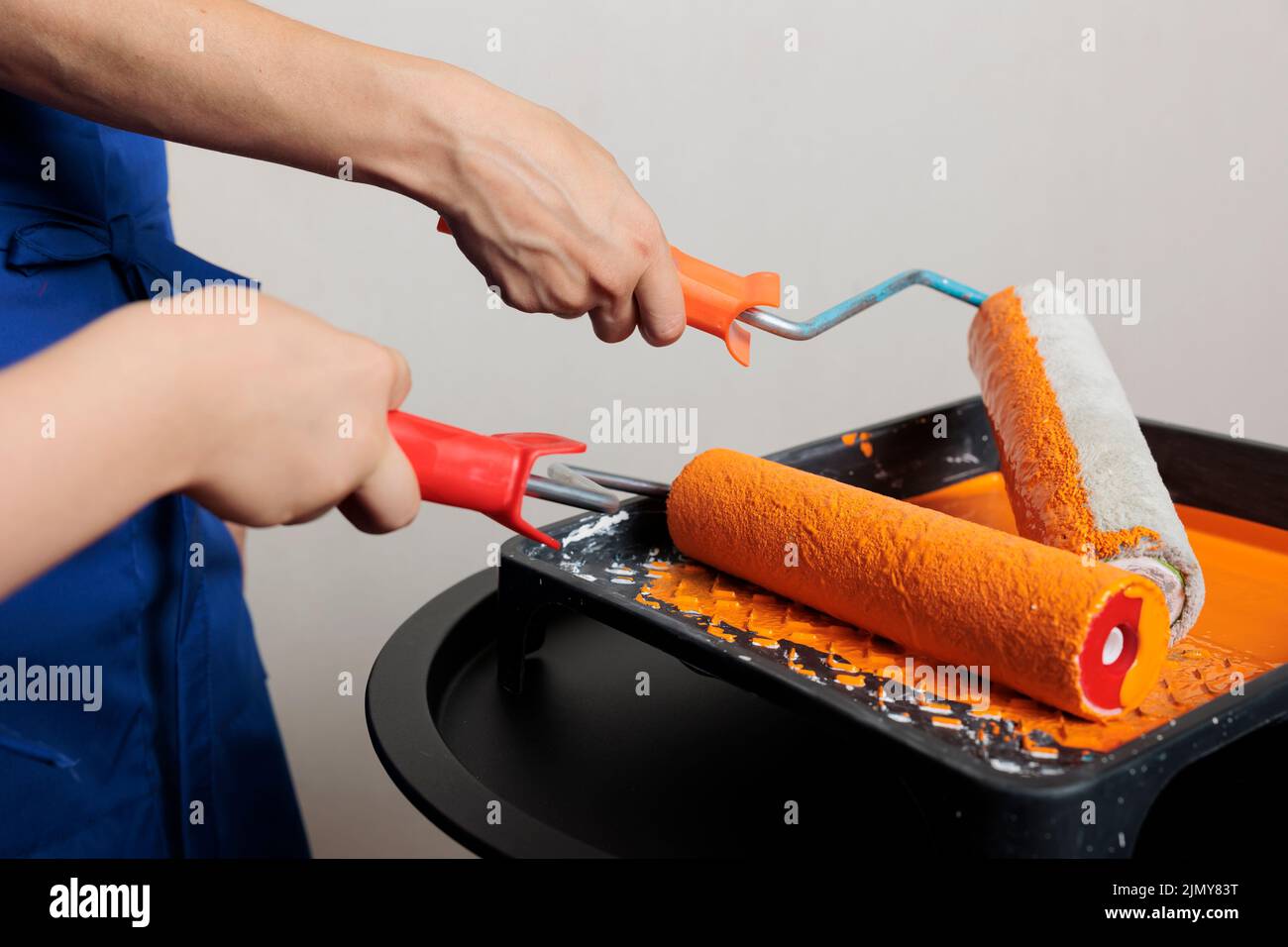 Woman and kid using roller brush and orange paint to renovate apartment ...