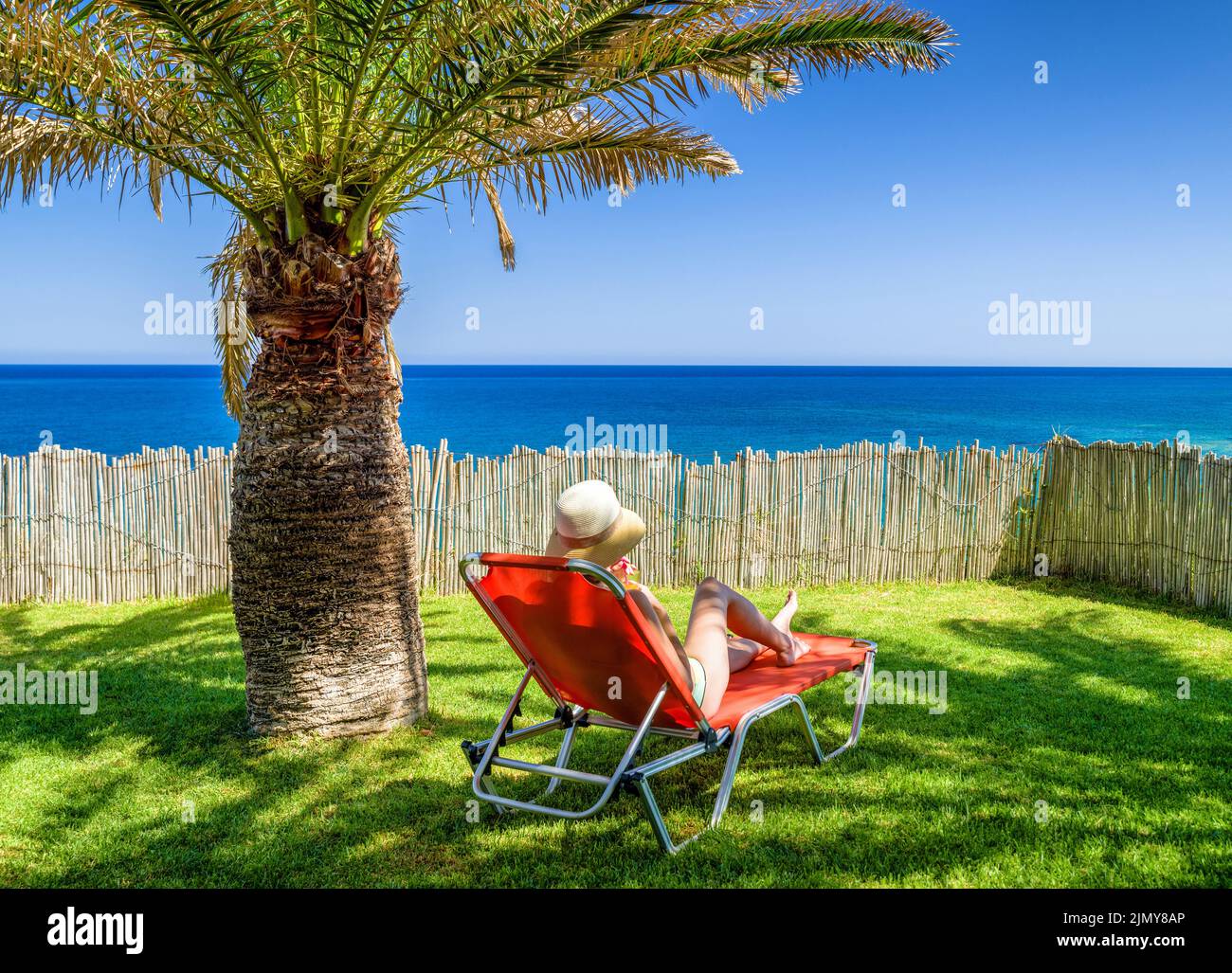 Woman With Sunhat Lying On Lounger In Exotic Tropical Resort Under Palm