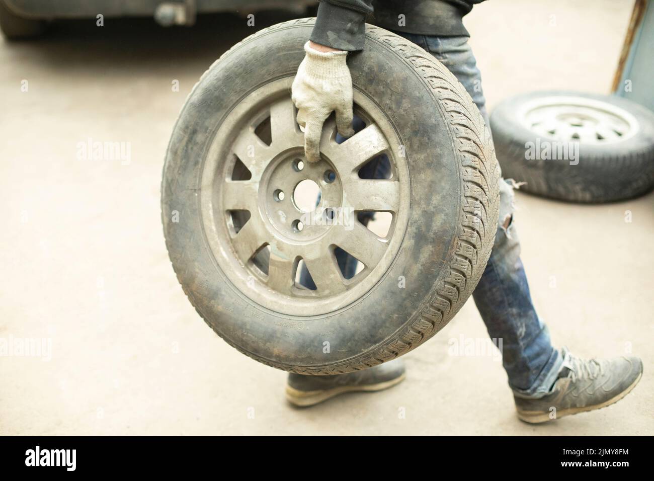 Guy changes wheel. Man carries wheel from car in his hand. Person makes ...