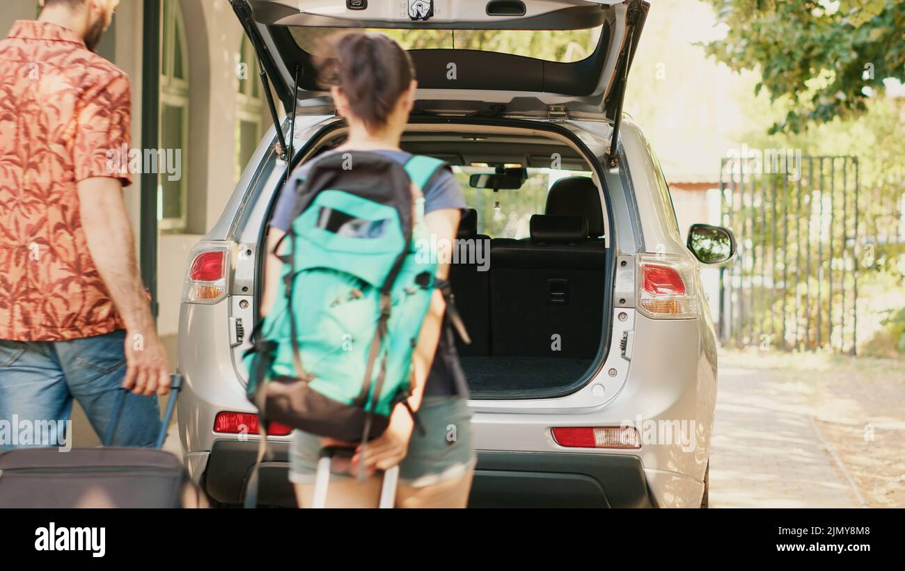 Casual couple putting voyage baggage inside vehicle trunk while getting ...