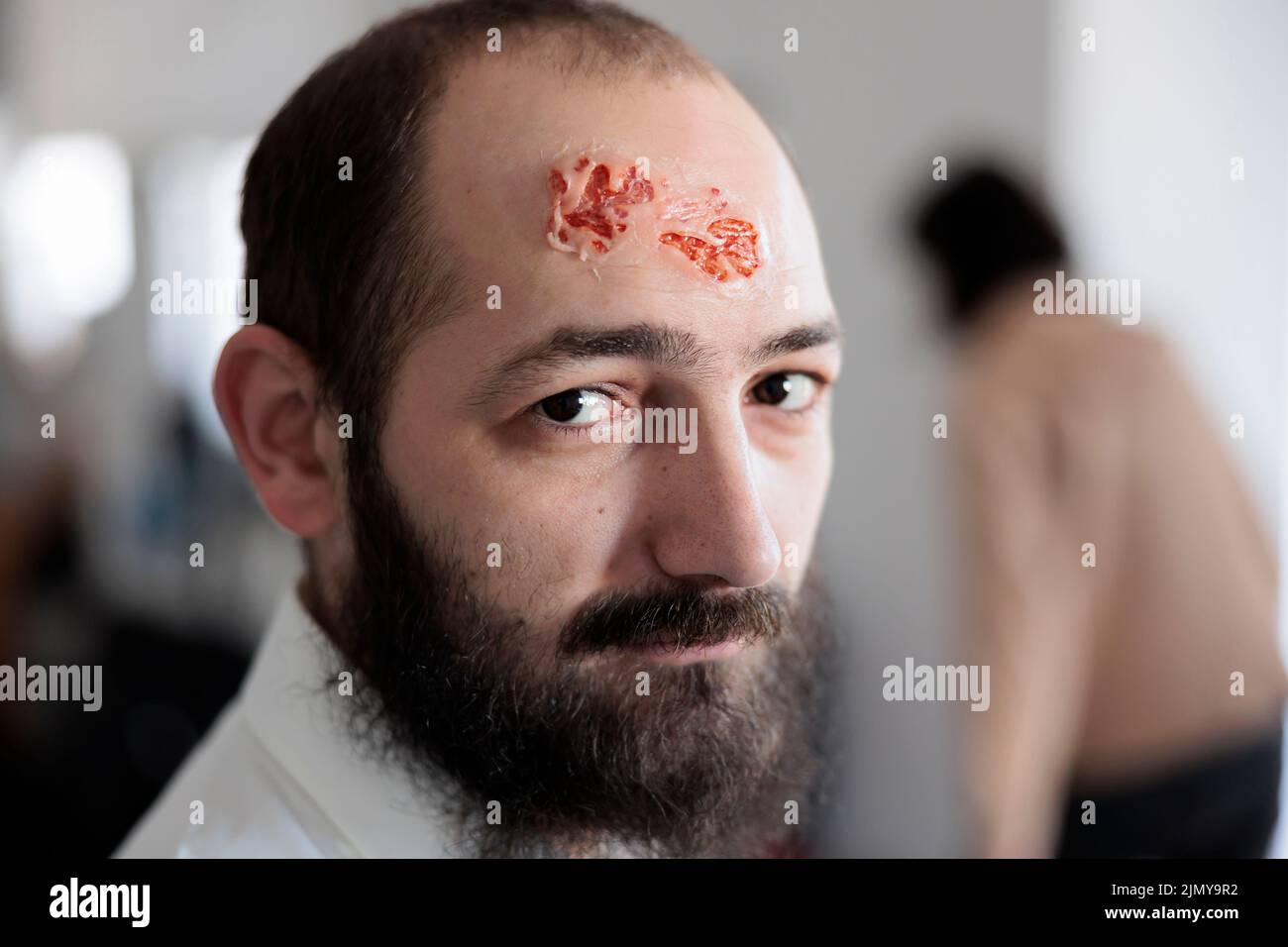 Portrait of man with bloody zombie wound, artist preparing makeup look ...