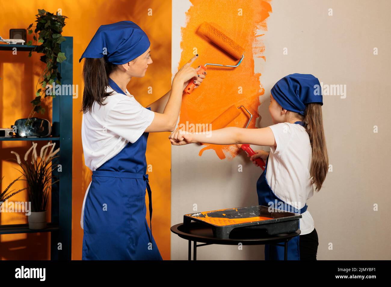Mother and girl painting house walls with orange color paint, using ...