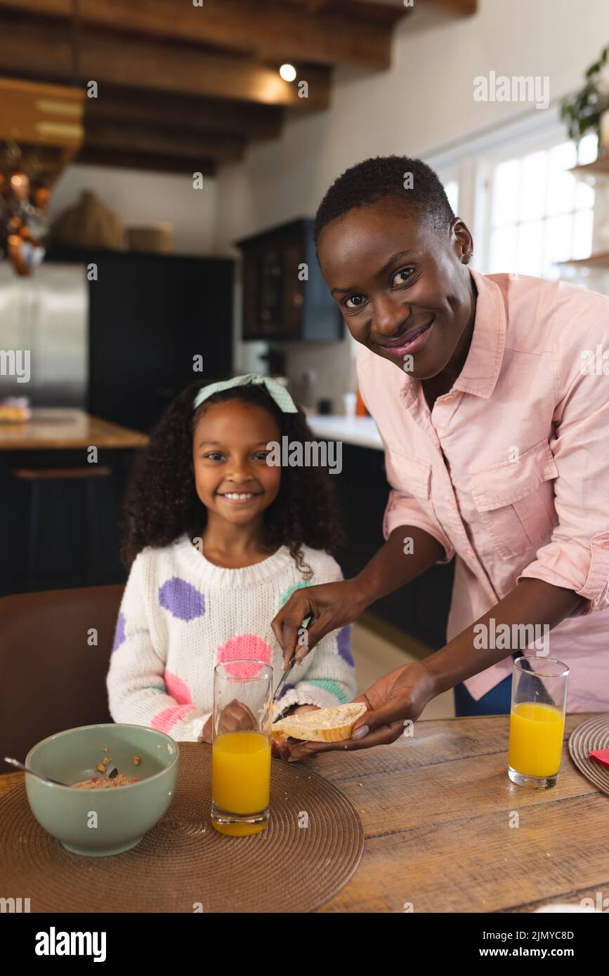 Vertical image of happy african american girl eating breakfast with mother Stock Photo - Alamy