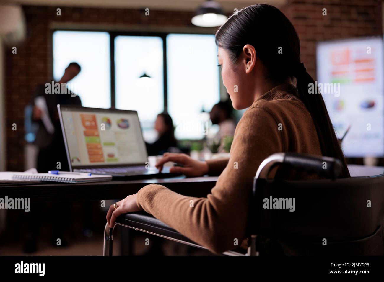 Asian employee with physical impairment sitting in wheelchair, working ...