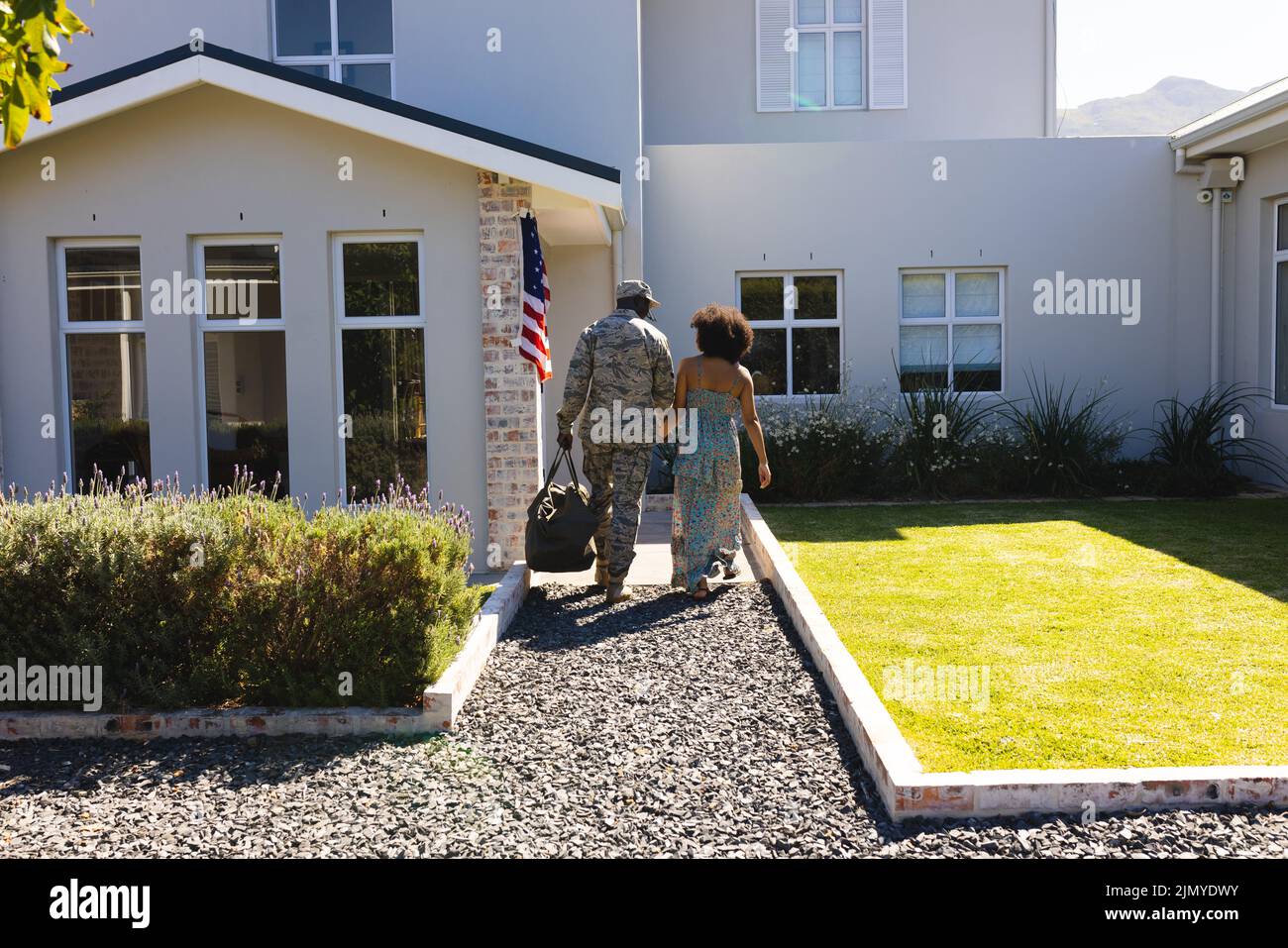Rear view of multiracial army soldier in camouflage holding wife's hand ...