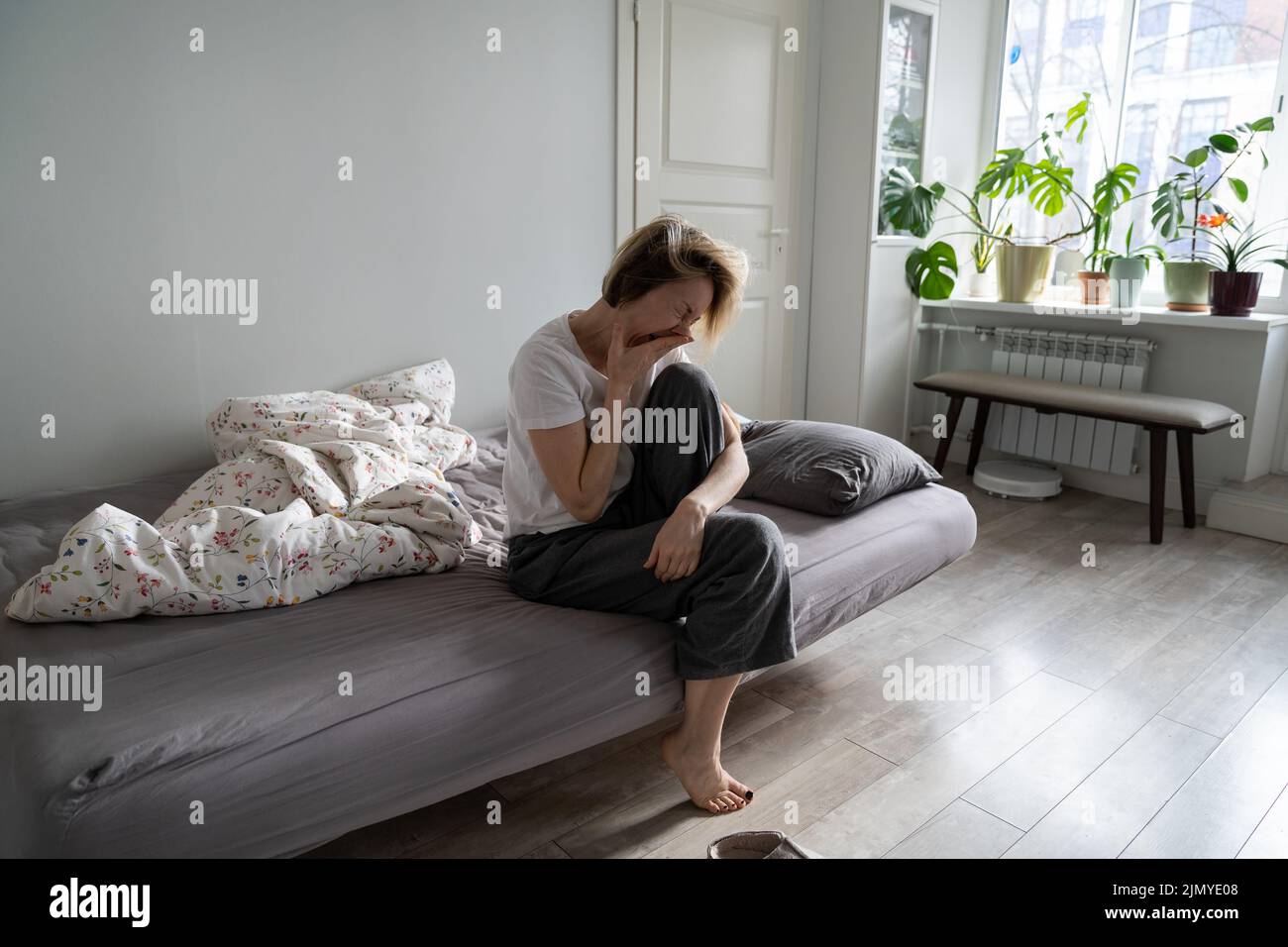 Depressed middle-aged woman sits on uncovered bed yawning after lonely ...