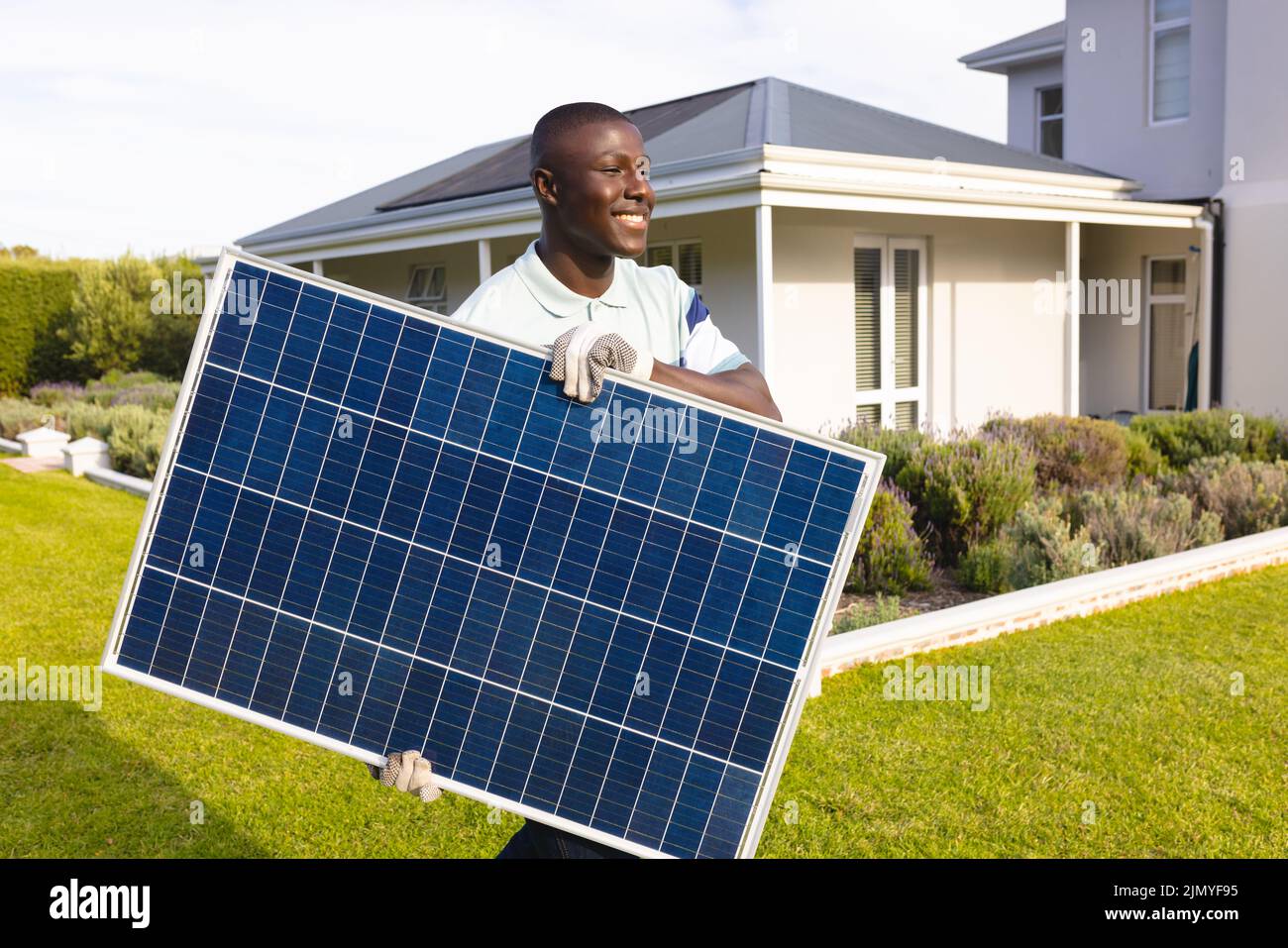 Smiling african american mid adult man carrying solar panel while ...
