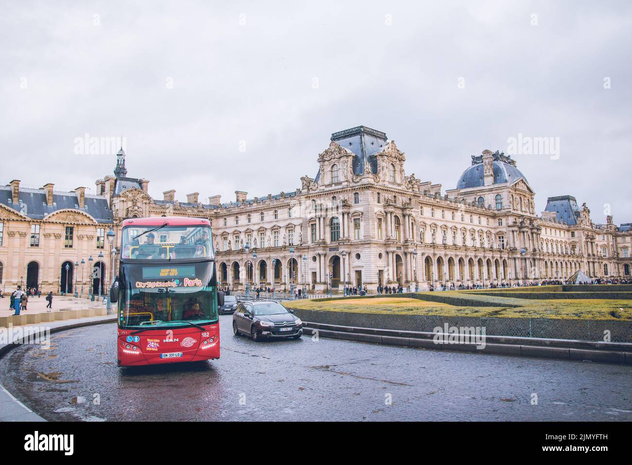 A cityscape of a red double-decker bus in front of the Louvre Museum in ...