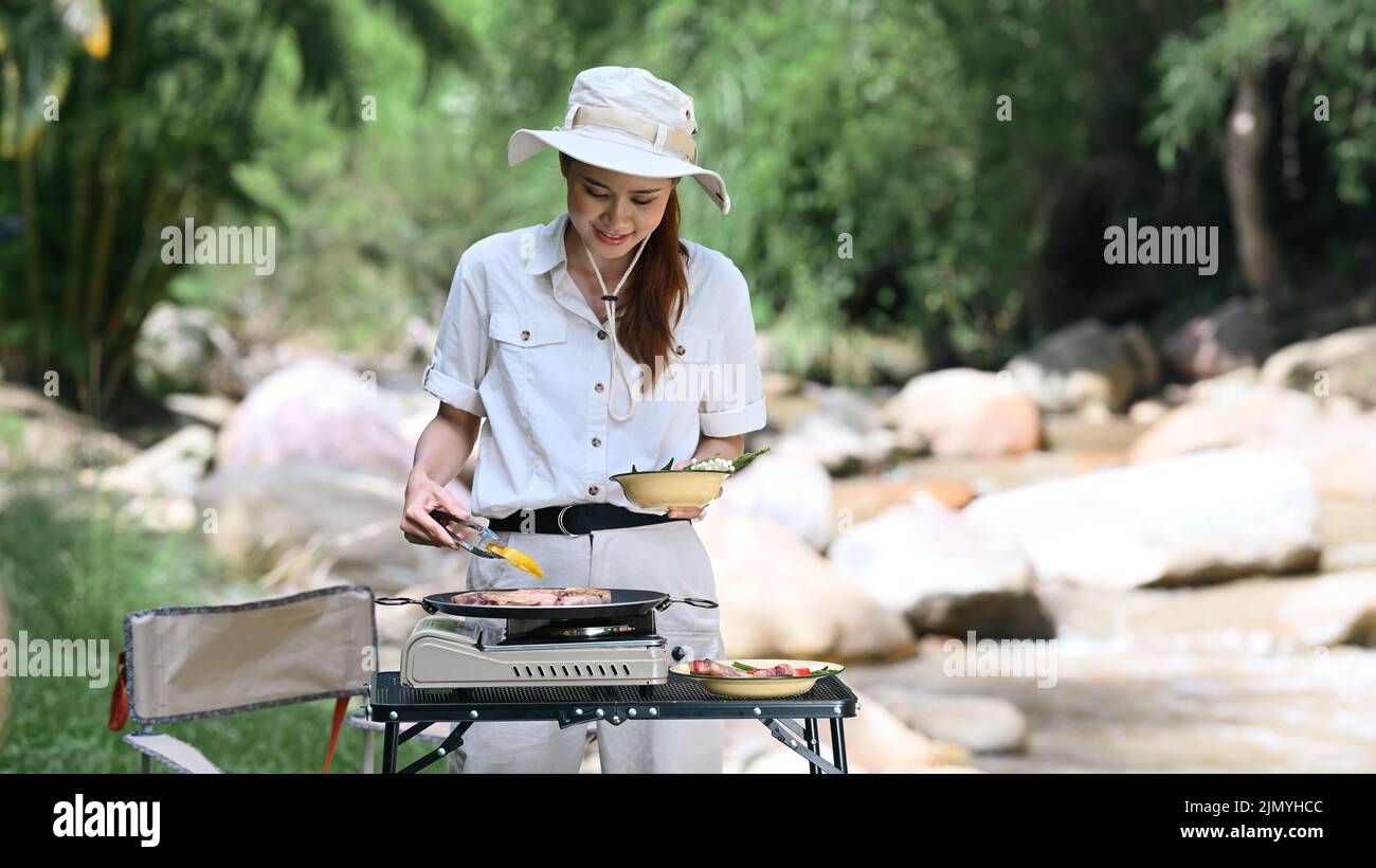 Young woman grilling meat on a portable gas stove while camping in ...