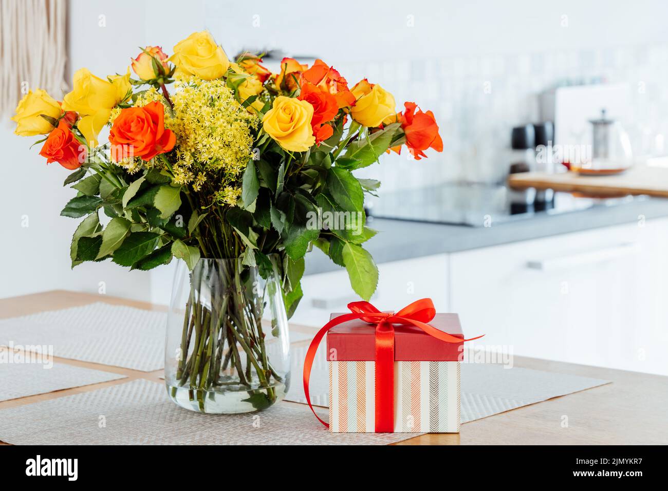 Yellow and orange roses in a vase and gift box with red ribbon on ...