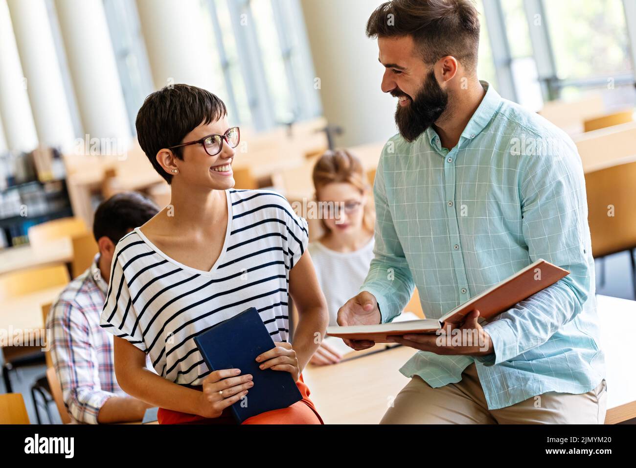 Happy young university students studying with books in library. Group ...