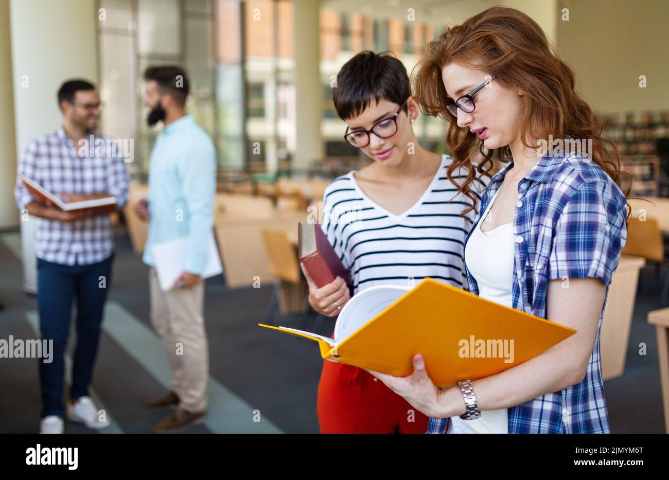 Happy university students studying with books in library. Group of ...