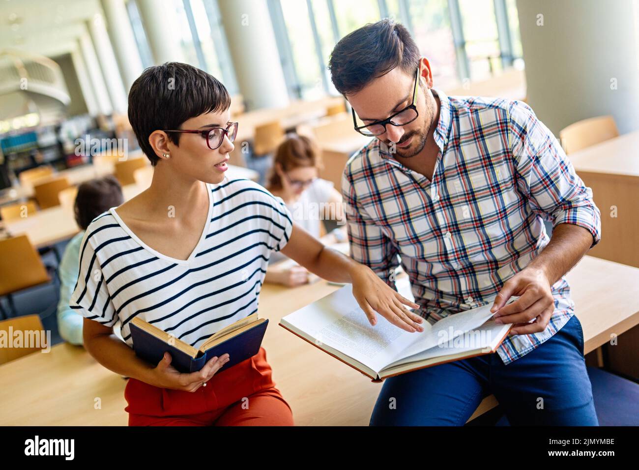 Happy university students studying with books in library. Group of ...