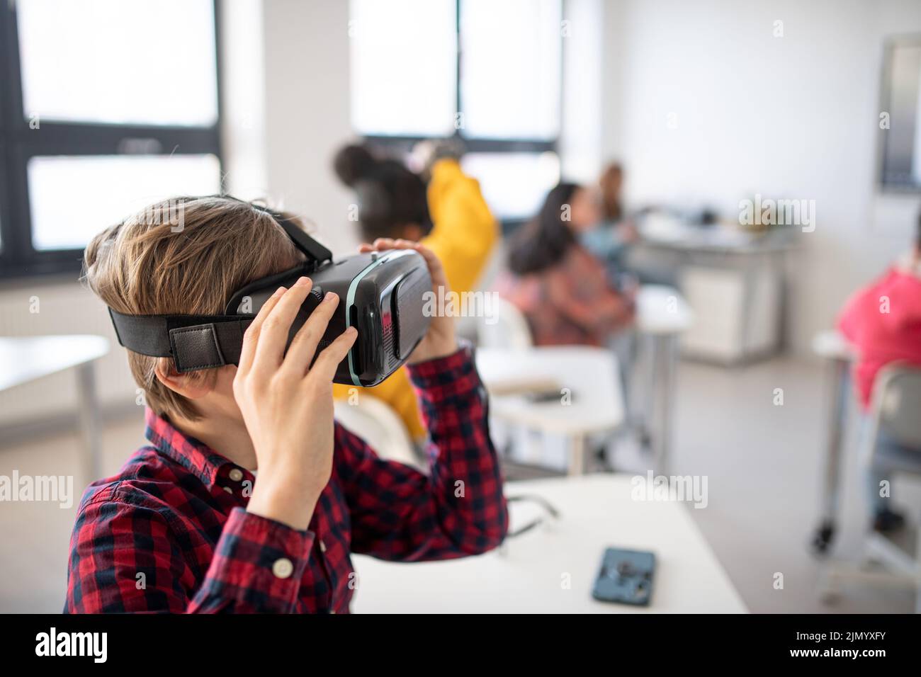 Curious student wearing virtual reality goggles at school in computer ...