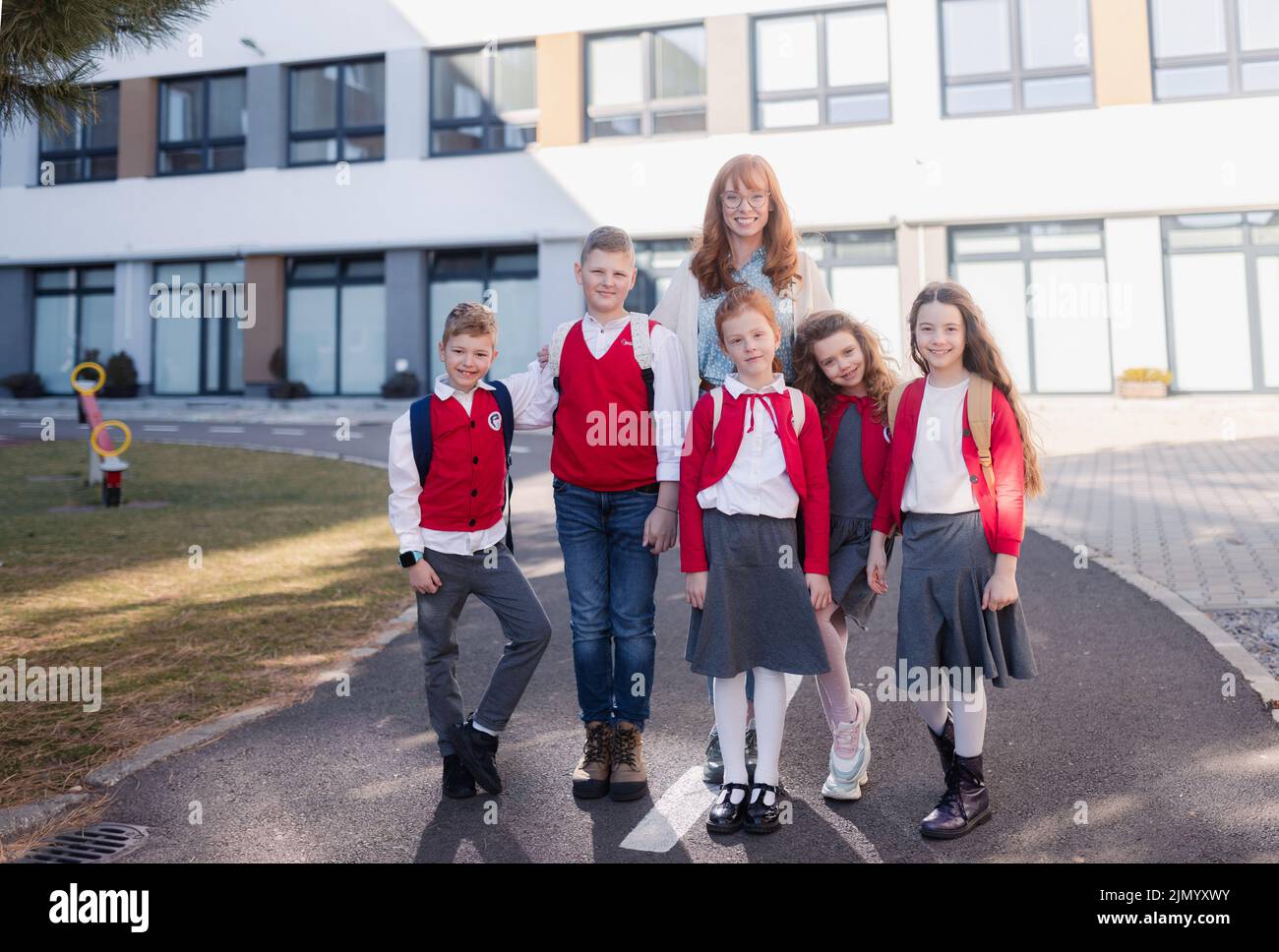 Portrait of happy schoolkids in uniforms with teacher at schoolyard ...