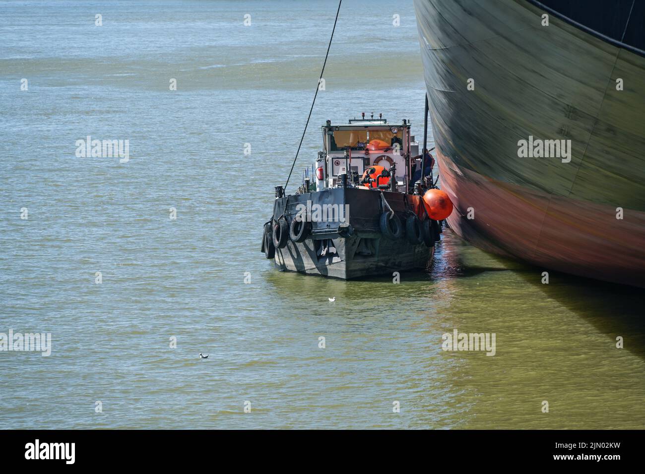 Small tanker boat or bunker barge at the hull of a large container ship ...