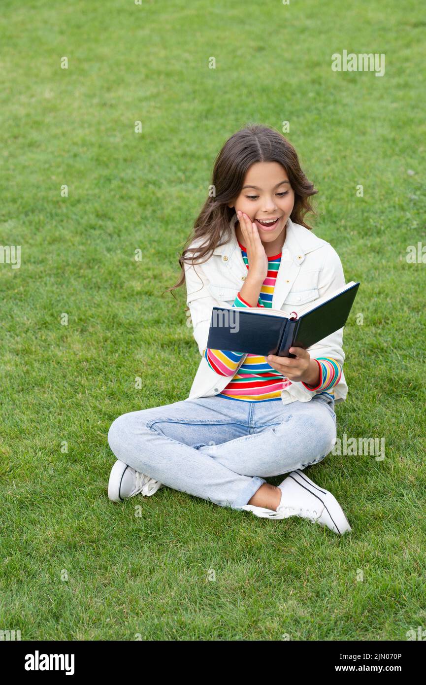 surprised teen child read book sitting on grass. reading book. reader ...