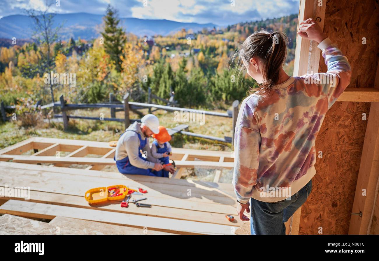 Father, mother and son building wooden frame house. Toddler boy helping ...