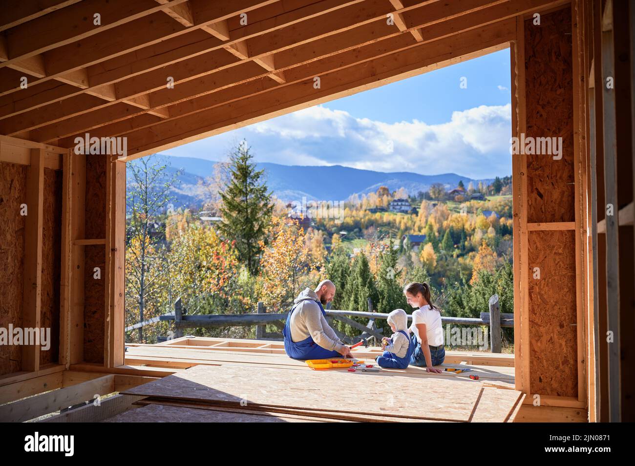 Father, mother and son building wooden frame house. Toddler boy helping ...
