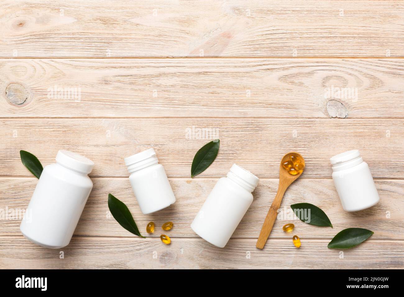 Omega-3 capsules lie in white bottle on a table with green leaves ...