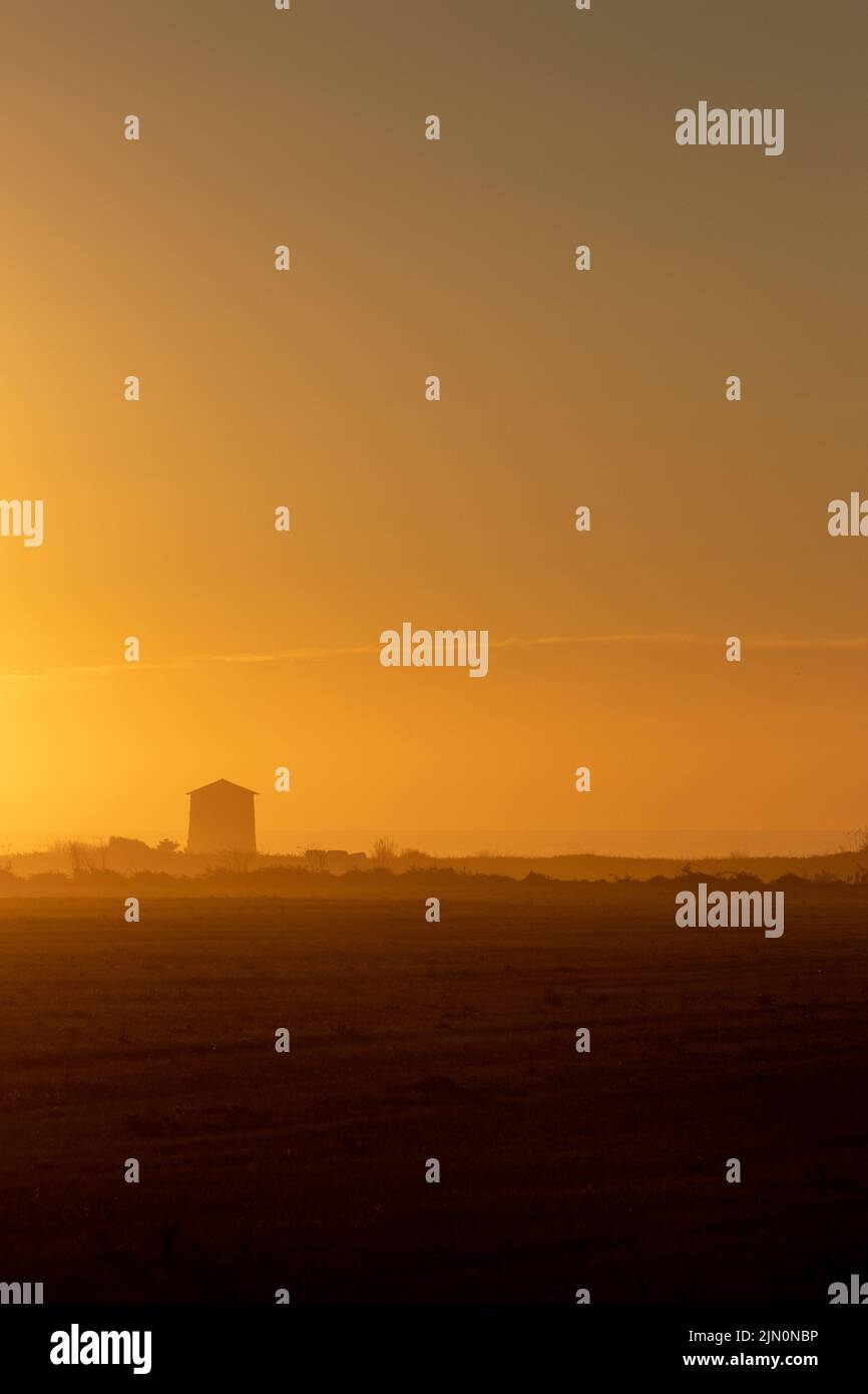 A vertical shot of the silhouette of a mill in the distance at sunset ...
