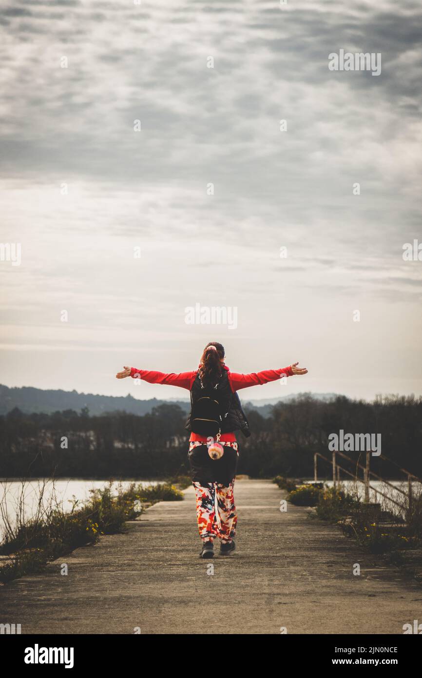 A vertical shot of a woman walking down a path with her arms ...