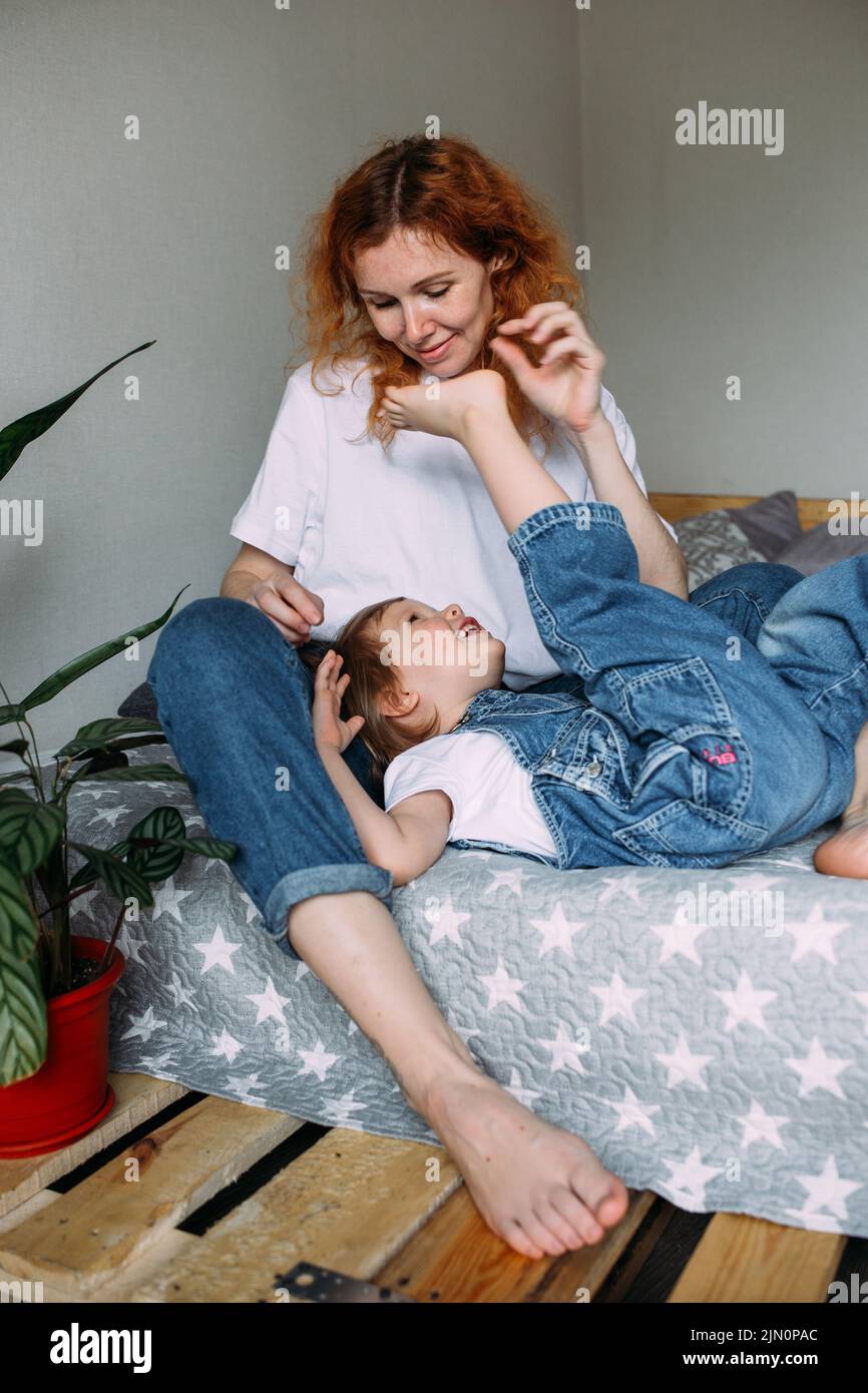 Young mother and child have fun and fool around at home on the bed ...