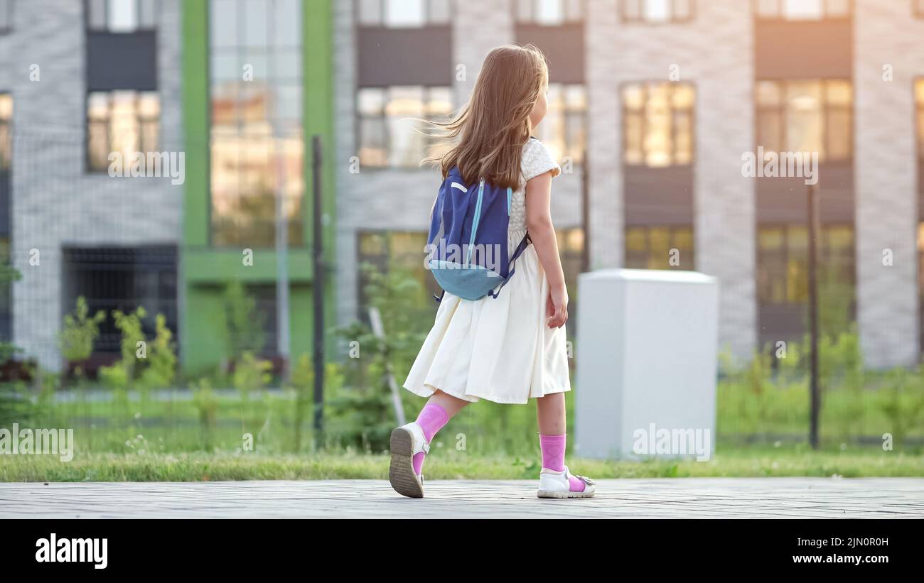 Preschooler girl with schoolbag walks past school building Stock Photo ...