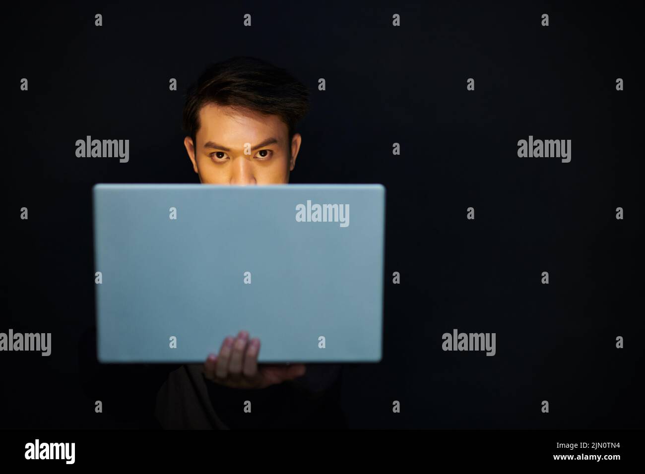 Serious hacker looking at camera over laptop screen when working in ...
